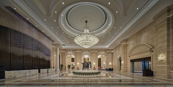 Um hall amplo com um lustre imponente, piso de mármore e arquitetura clássica.