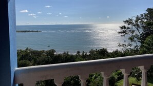 Varanda com vista para o mar, uma ilha ao longe e vegetação exuberante.