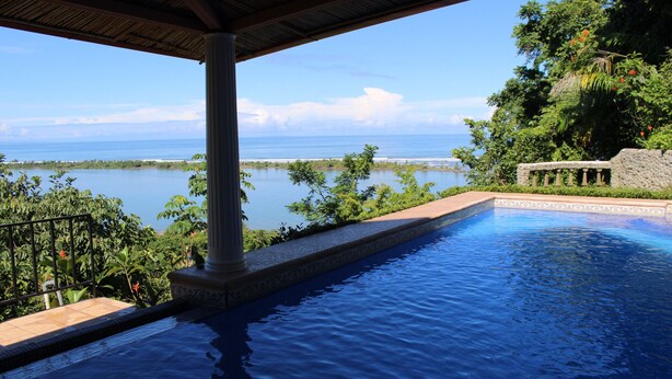 Piscina com vista para o oceano e área coberta com um pilar.