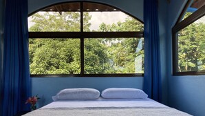Quarto com uma janela grande, cama com roupa de cama branca e cortinas azuis.