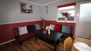 Uma sala de estar com esquema de cores vermelho e branco, um sofá, uma mesa de centro, uma mesa de jantar com cadeiras e uma janela com vista.