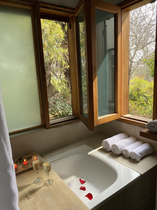 Casa de banho com banheira, duas velas e janela com vista para vegetação.