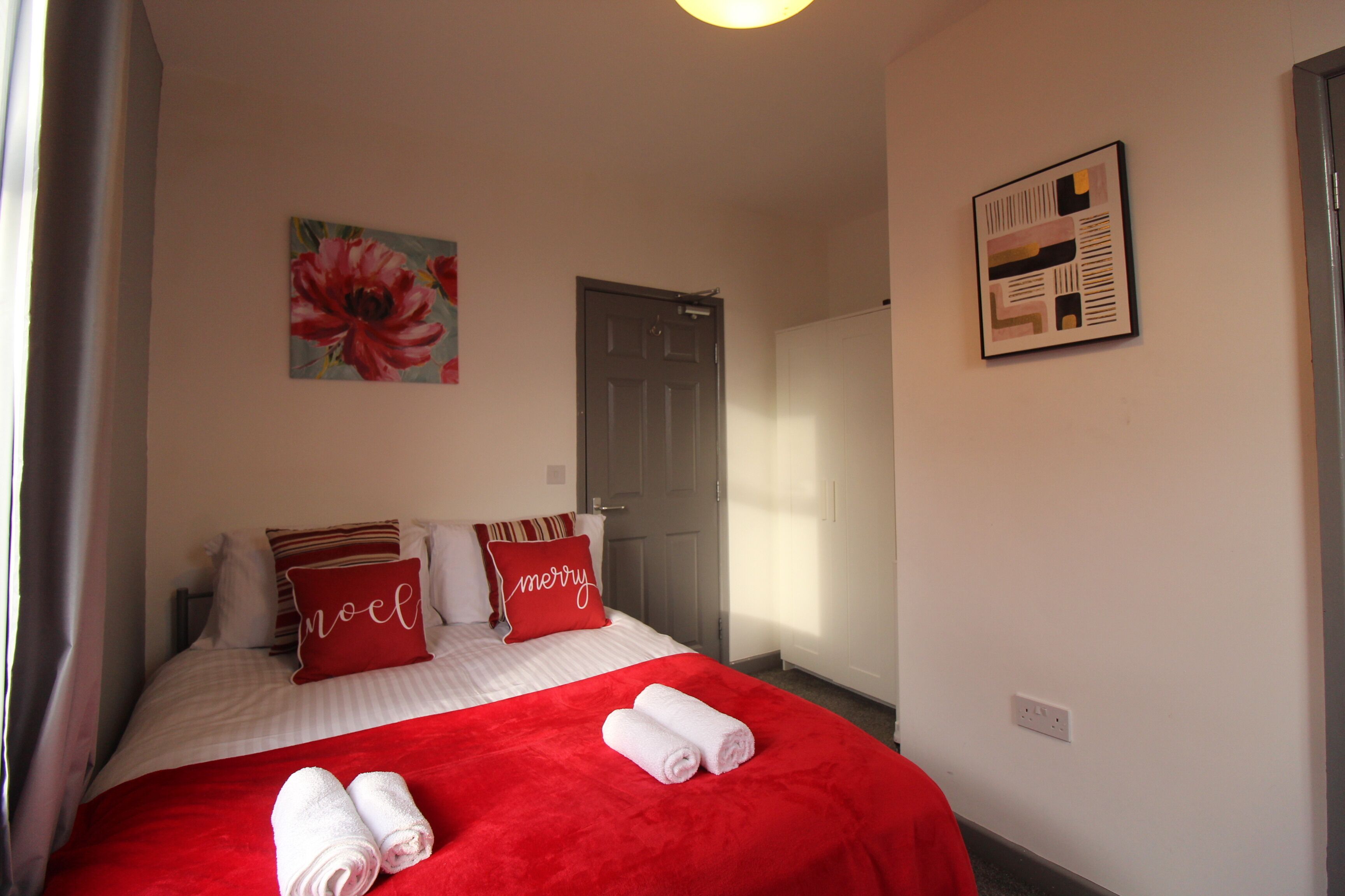 Quarto de hotel com cama, roupa de cama vermelha e branca, dois travesseiros vermelhos, um cobertor vermelho e dois toalhas enroladas na cama.