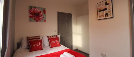 Quarto de hotel com cama, roupa de cama vermelha e branca, dois travesseiros vermelhos, um cobertor vermelho e dois toalhas enroladas na cama.