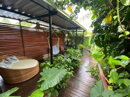 Uma área externa coberta com deck de madeira, uma cadeira suspensa e vegetação exuberante.