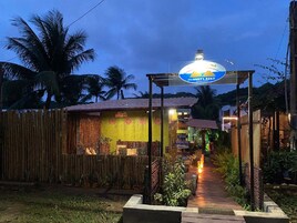 Um restaurante com uma placa indicando que é um estabelecimento NA, uma cerca de madeira e um caminho que leva à entrada.