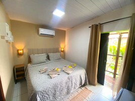 Quarto com cama, luminárias de cabeceira, ar-condicionado e vista através de uma porta.