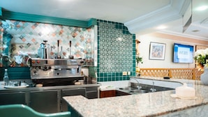 Cozinha com máquina de café, pia e painel de azulejos.