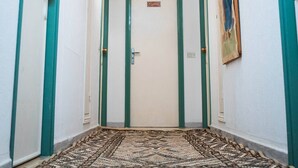 Corredor com portas de acabamento azul-esverdeado, tapete estampado e teto com design geométrico.