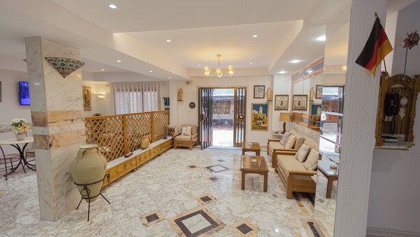 Uma sala de estar ampla com piso de mármore, um conjunto de sofás de madeira, uma mesinha de madeira e um vaso decorativo.