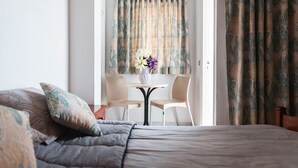 Quarto com cama, almofadas, uma mesinha redonda com cadeiras e cortinas.
