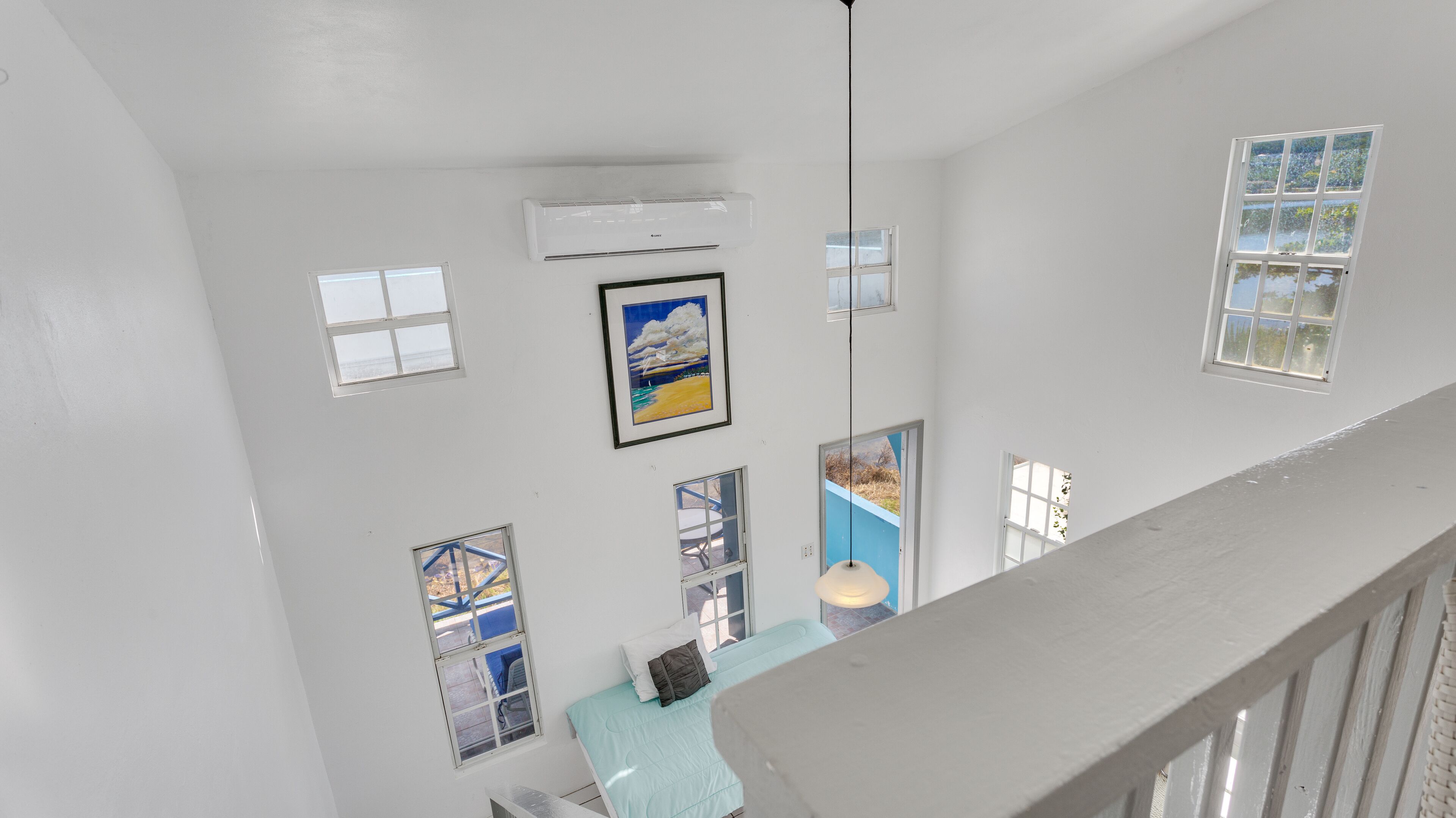 Quarto amplo com pé direito alto, várias janelas, cama e ventoinha no teto.