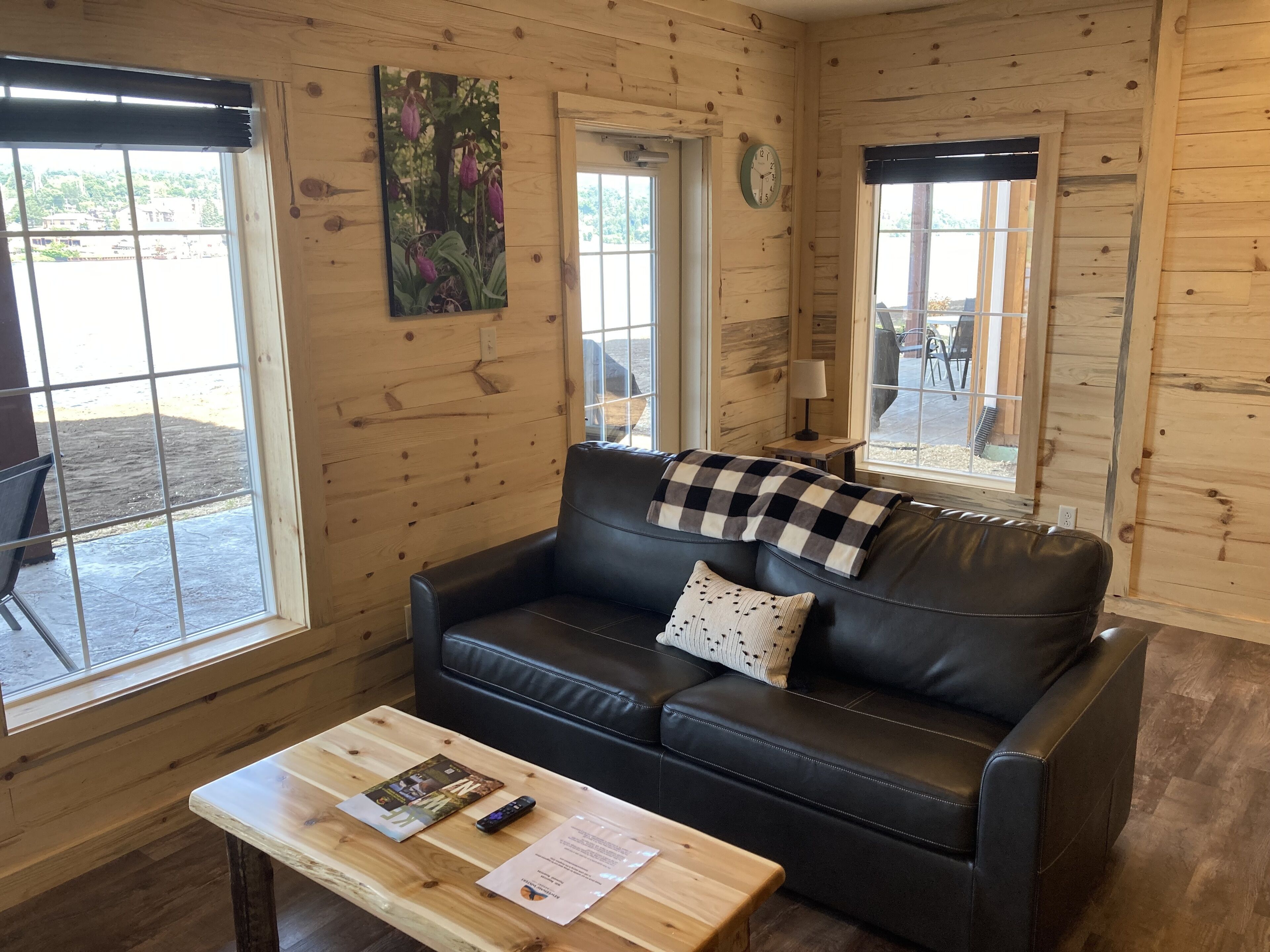 Um quarto acolhedor em estilo cabana, com um sofá de couro preto, uma mesa de centro de madeira e uma grande janela com vista para o exterior.