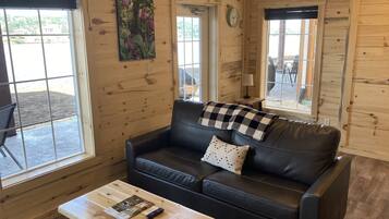 Um quarto acolhedor em estilo cabana, com um sofá de couro preto, uma mesa de centro de madeira e uma grande janela com vista para o exterior.