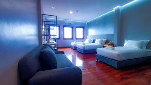 Quarto de hotel moderno com sofá, duas camas, escrivaninha e vista para o exterior.