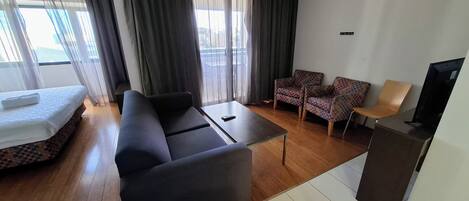 Quarto de hotel com cama, sofá, duas poltronas estampadas, uma mesinha e televisão.