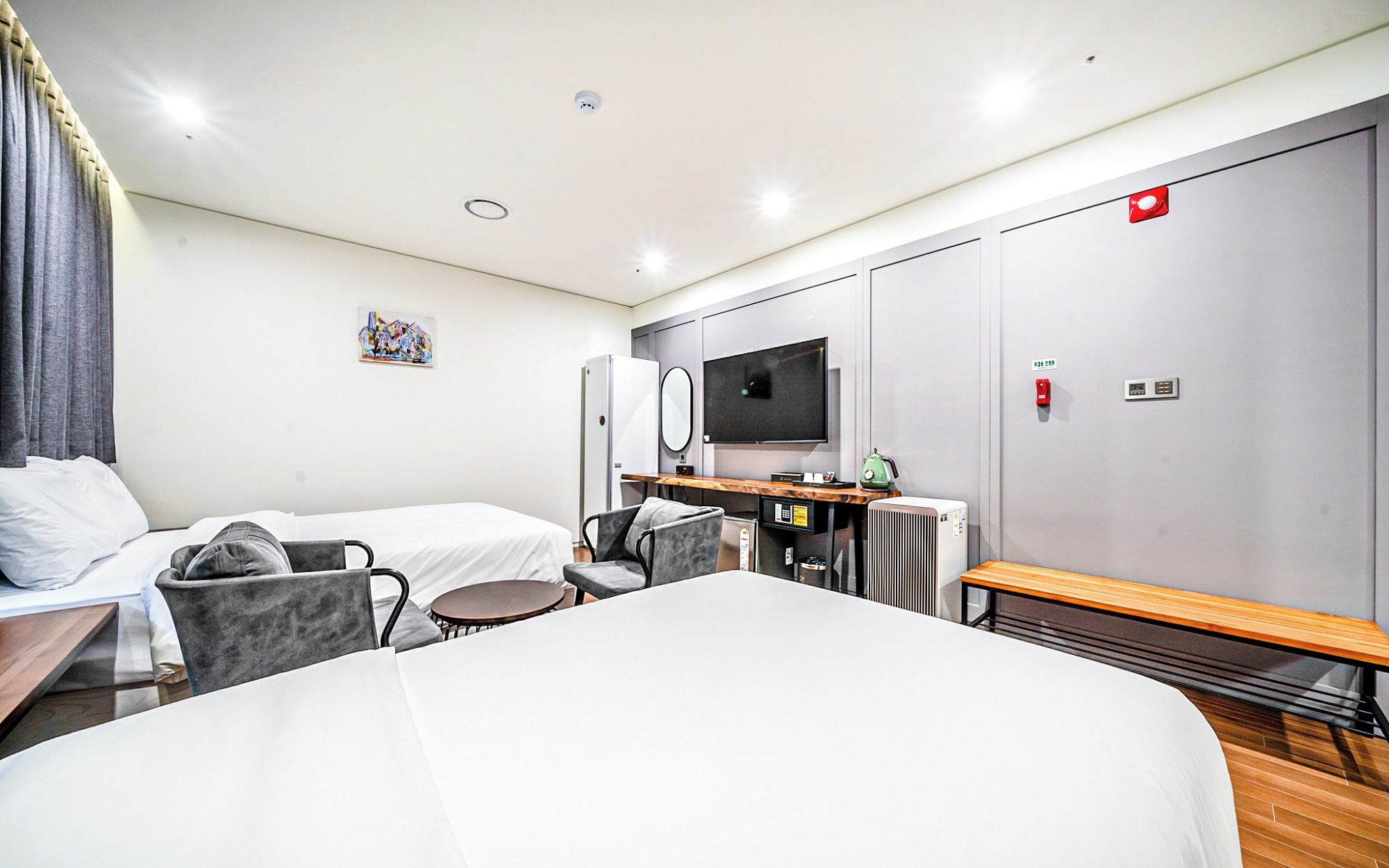 Quarto de hotel com cama, duas cadeiras, escrivaninha, televisão e guarda-roupa.