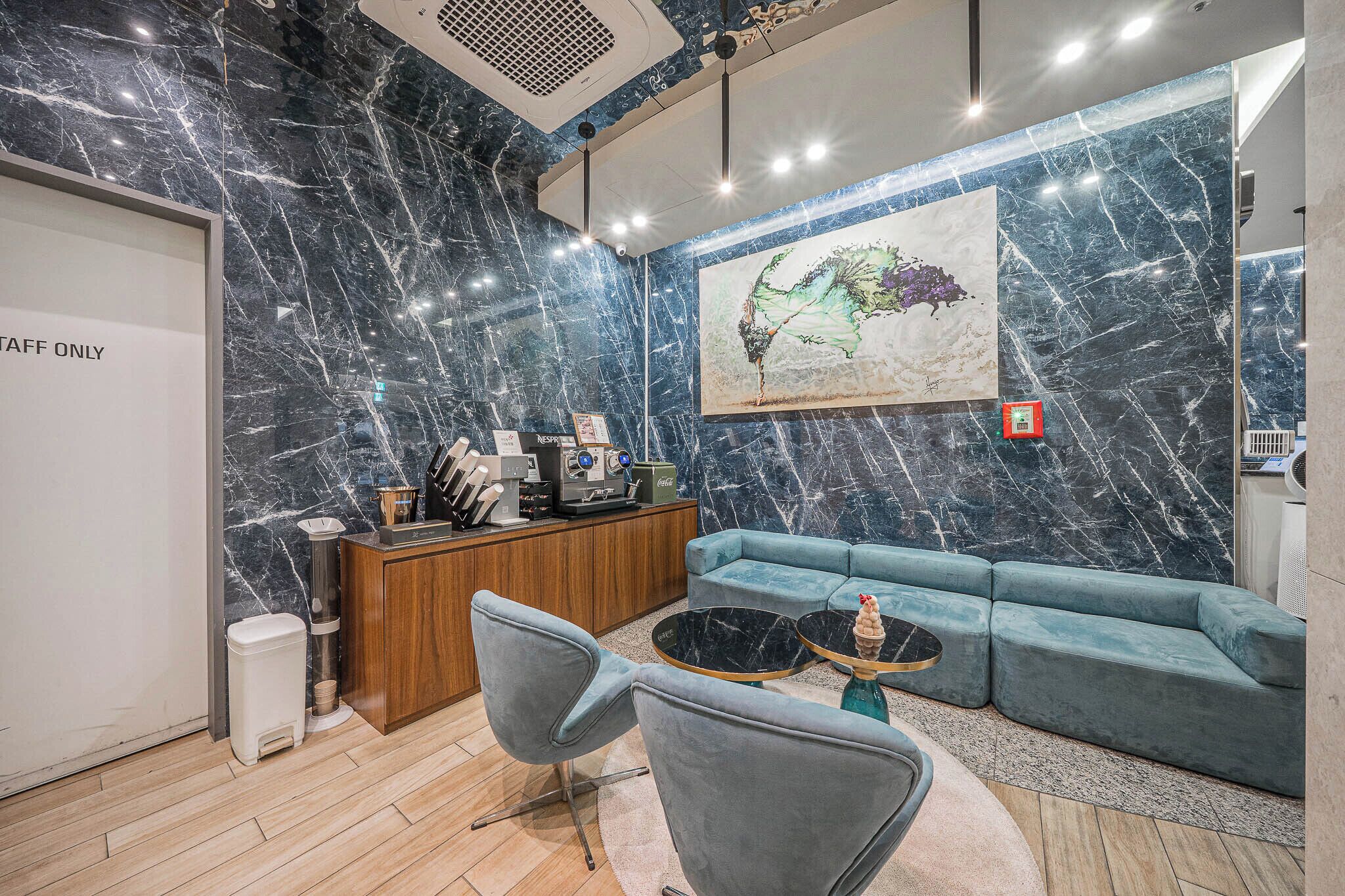 Um hall moderno com parede de mármore, balcão de recepção, sofá azul e uma máquina de café.