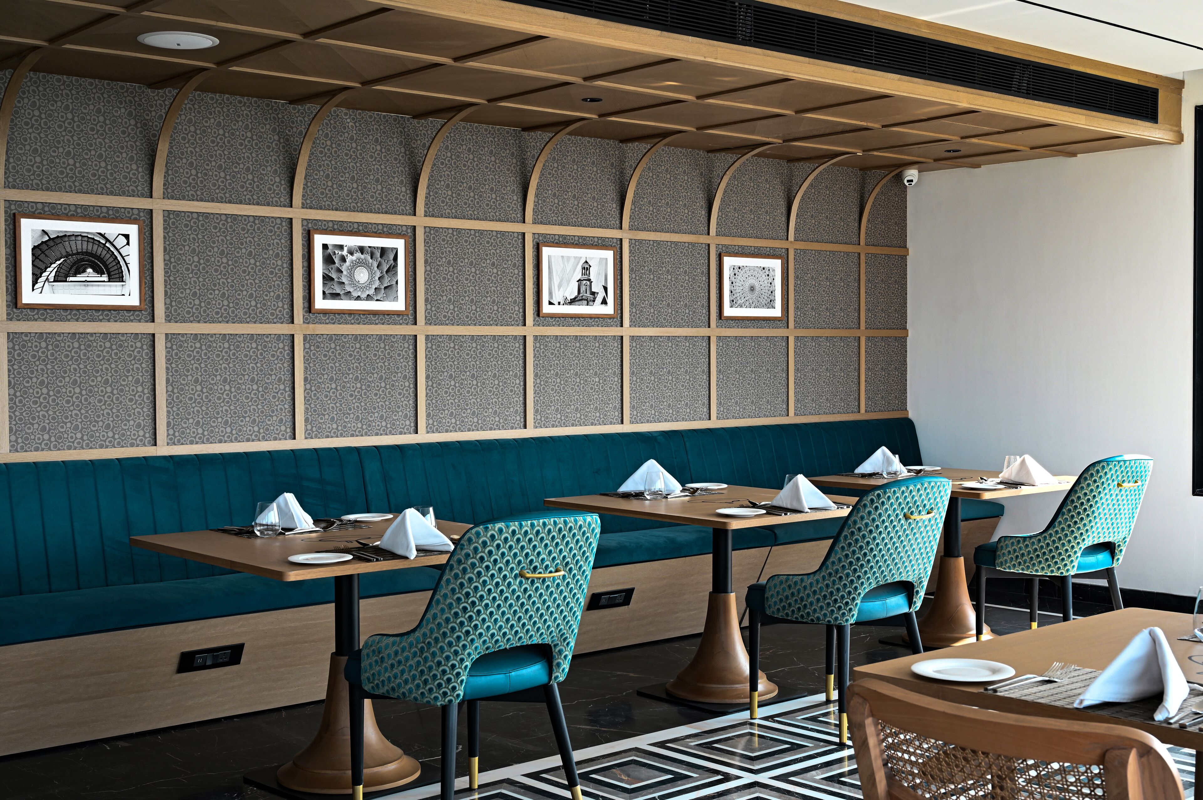 Restaurante com assentos estofados em tons de verde-água e cadeiras estampadas, obras de arte emolduradas na parede e um design moderno no teto.