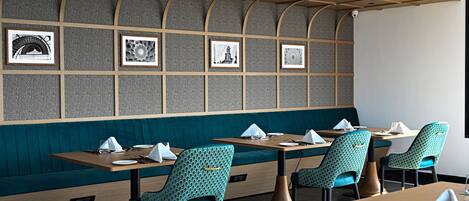 Restaurante com assentos estofados em tons de verde-água e cadeiras estampadas, obras de arte emolduradas na parede e um design moderno no teto.