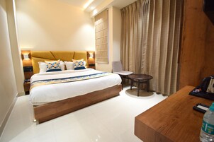 Quarto de hotel com uma cama grande, mesas de cabeceira, uma mesinha redonda e uma escrivaninha de madeira.