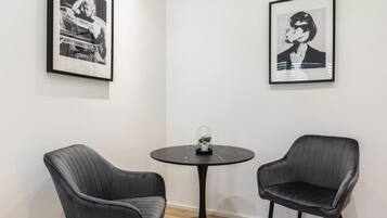 Quarto com duas cadeiras pretas, uma pequena mesa redonda e duas fotografias a preto e branco em molduras nas paredes.