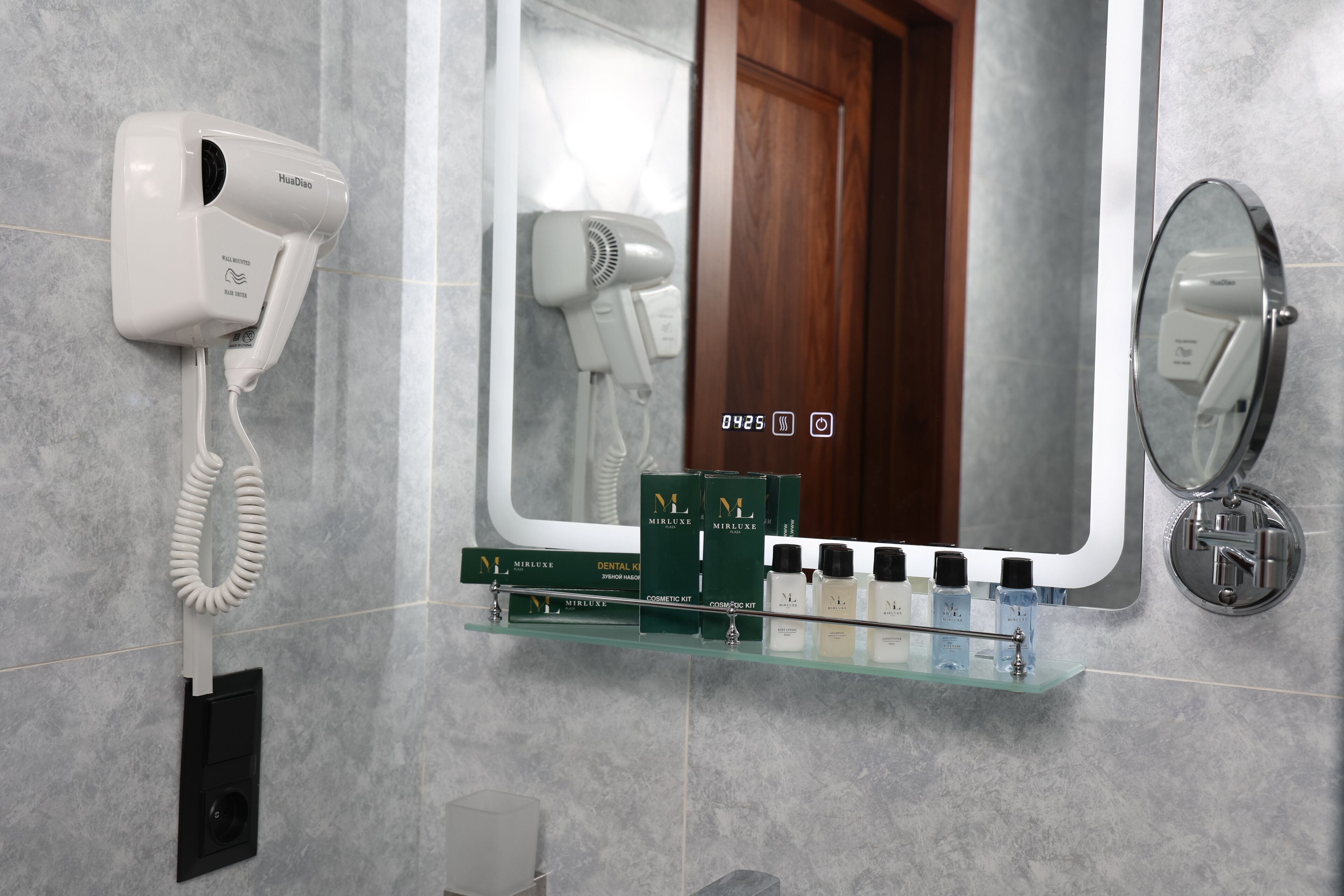 Casa de banho com secador de cabelo, espelho e prateleira com artigos de higiene pessoal.