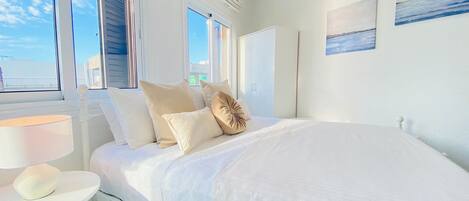 Um quarto com cama, mesa de cabeceira, janela e um quadro na parede.