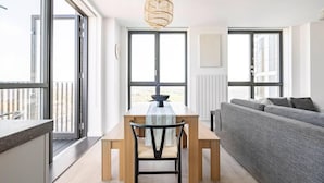 Uma sala de estar moderna com uma mesa de jantar de madeira, um sofá cinza e grandes janelas.