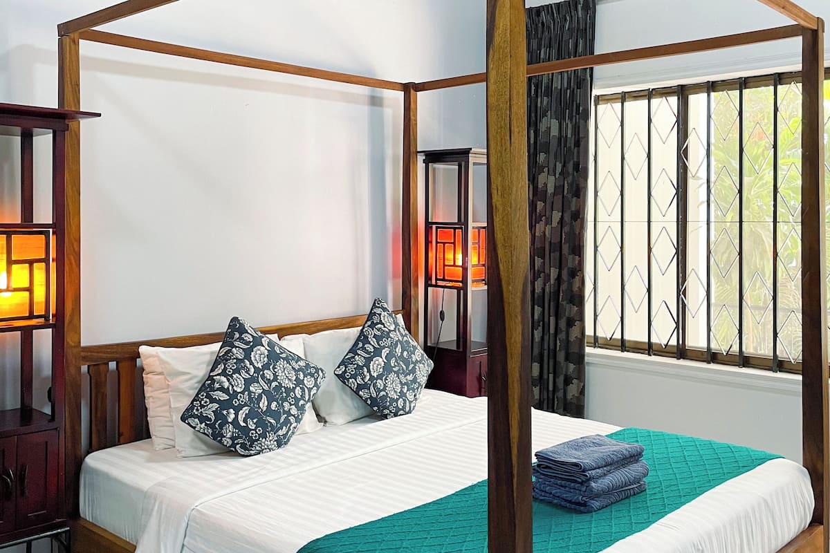 Uma cama com dossel de madeira, roupa de cama branca e um cobertor azul-esverdeado.