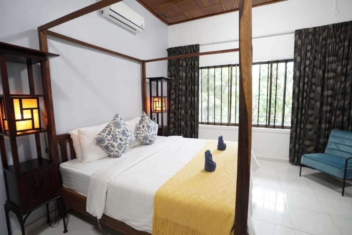 Quarto com cama de dossel, mesa de cabeceira, abajur, cadeira e janela com cortinas.