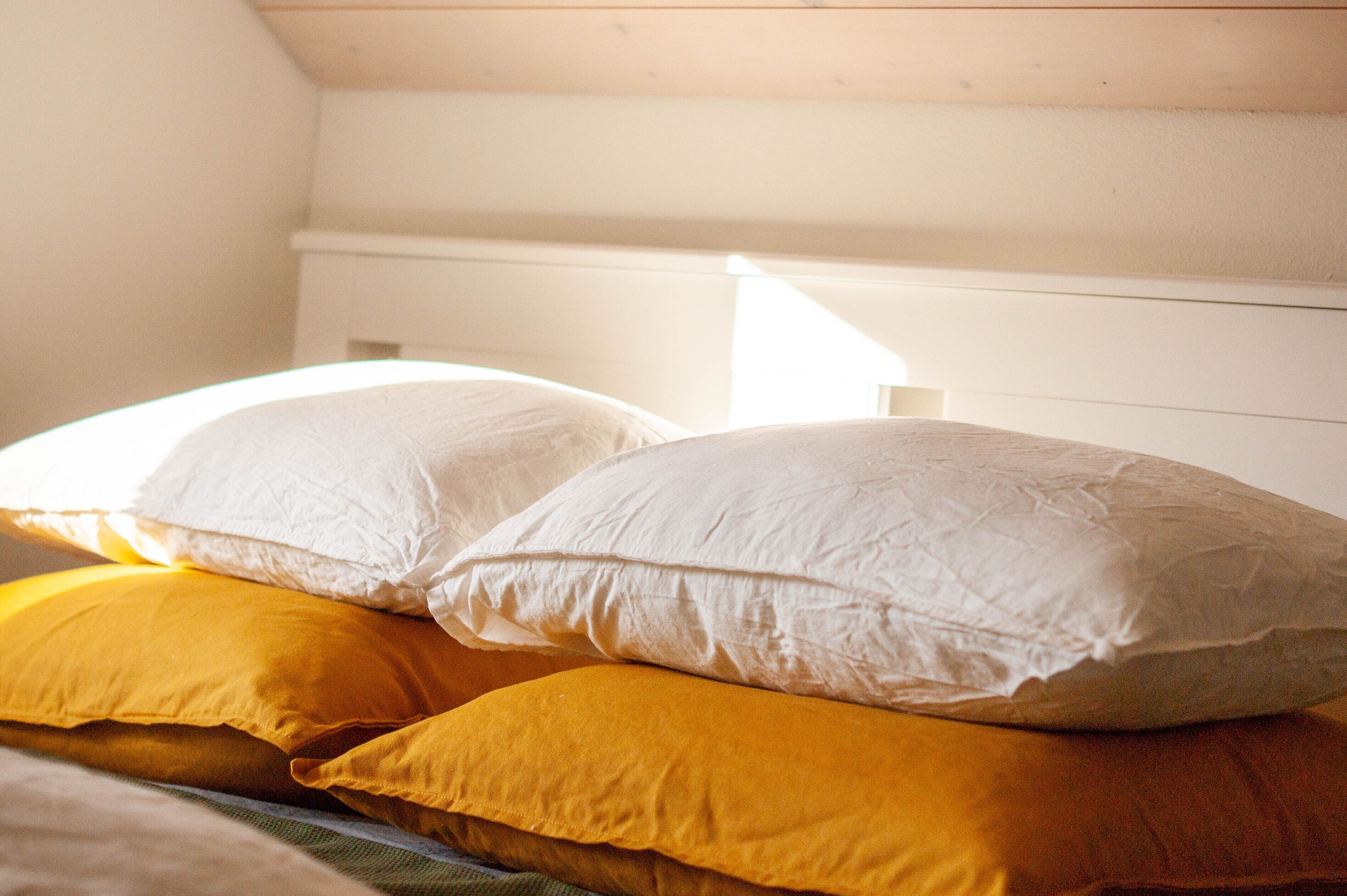 Cama com almofadas brancas e mostarda.