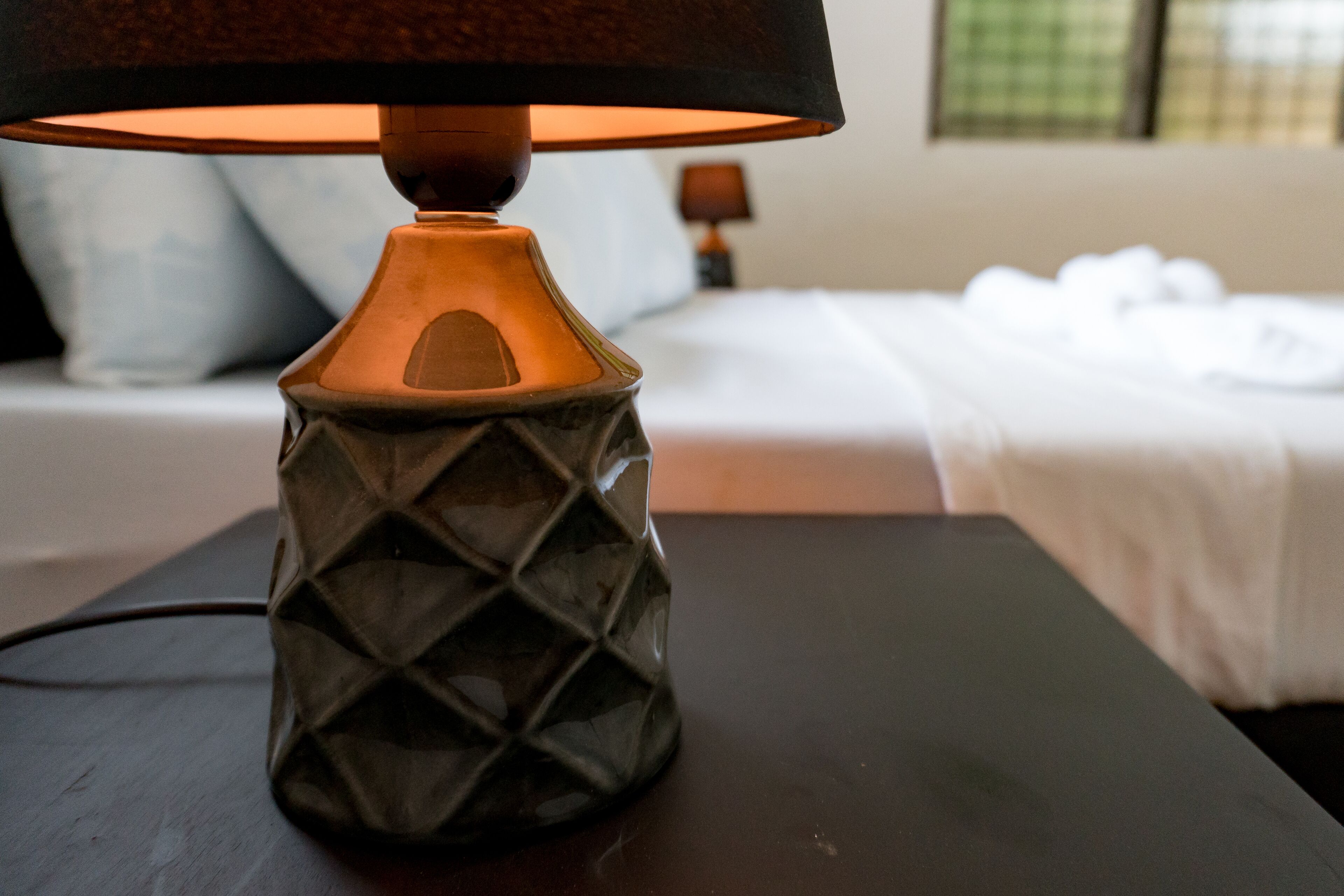 Uma luminária moderna com padrão geométrico sobre uma mesa de cabeceira em quarto de hotel.