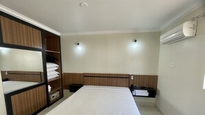 Quarto de hotel com beliches, uma cama de solteiro, mesa de cabeceira, luminária, ar condicionado e telefone fixo na parede.