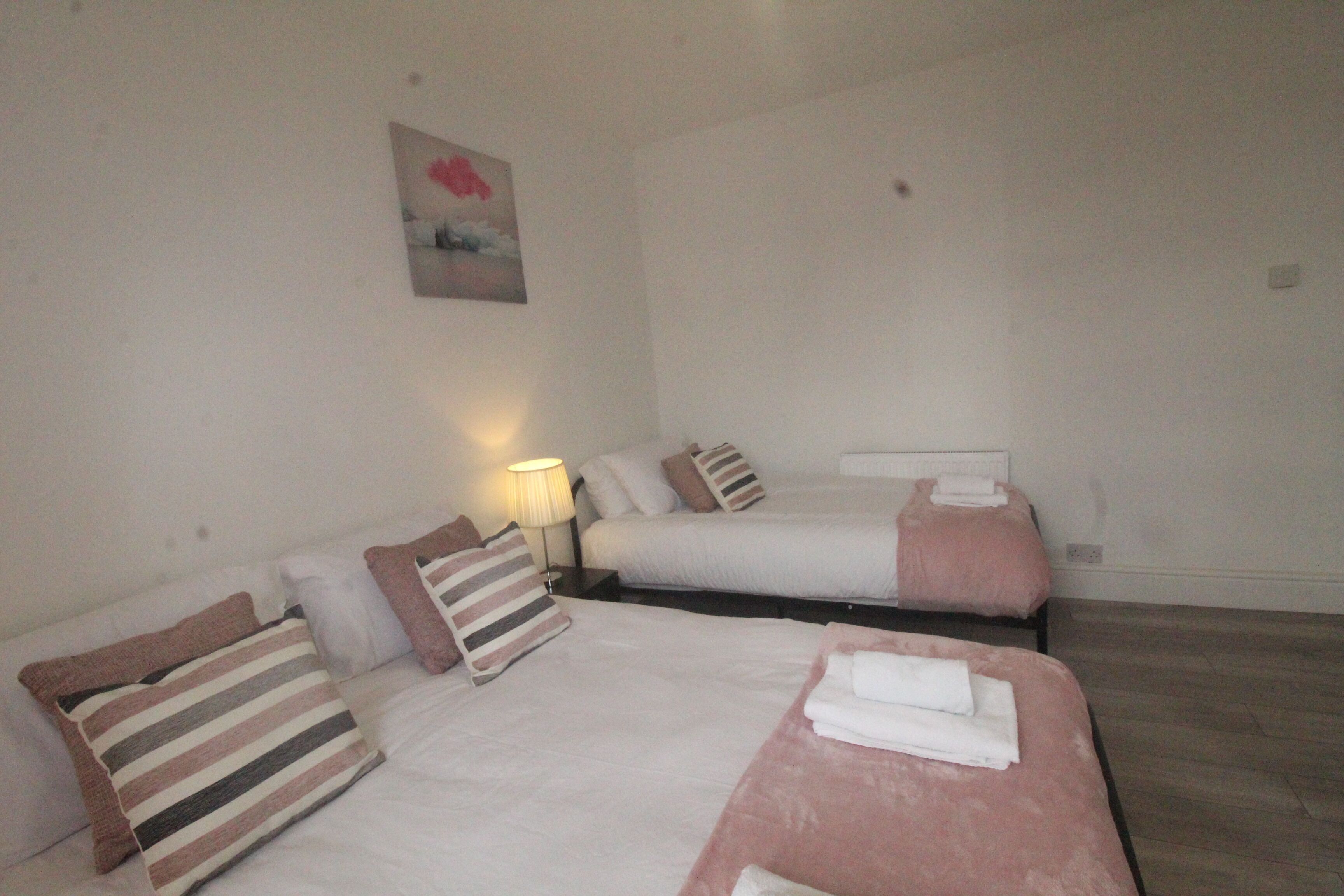 Quarto de hotel com duas camas, cada uma com almofadas listradas, uma luminária de cabeceira e um quadro na parede.