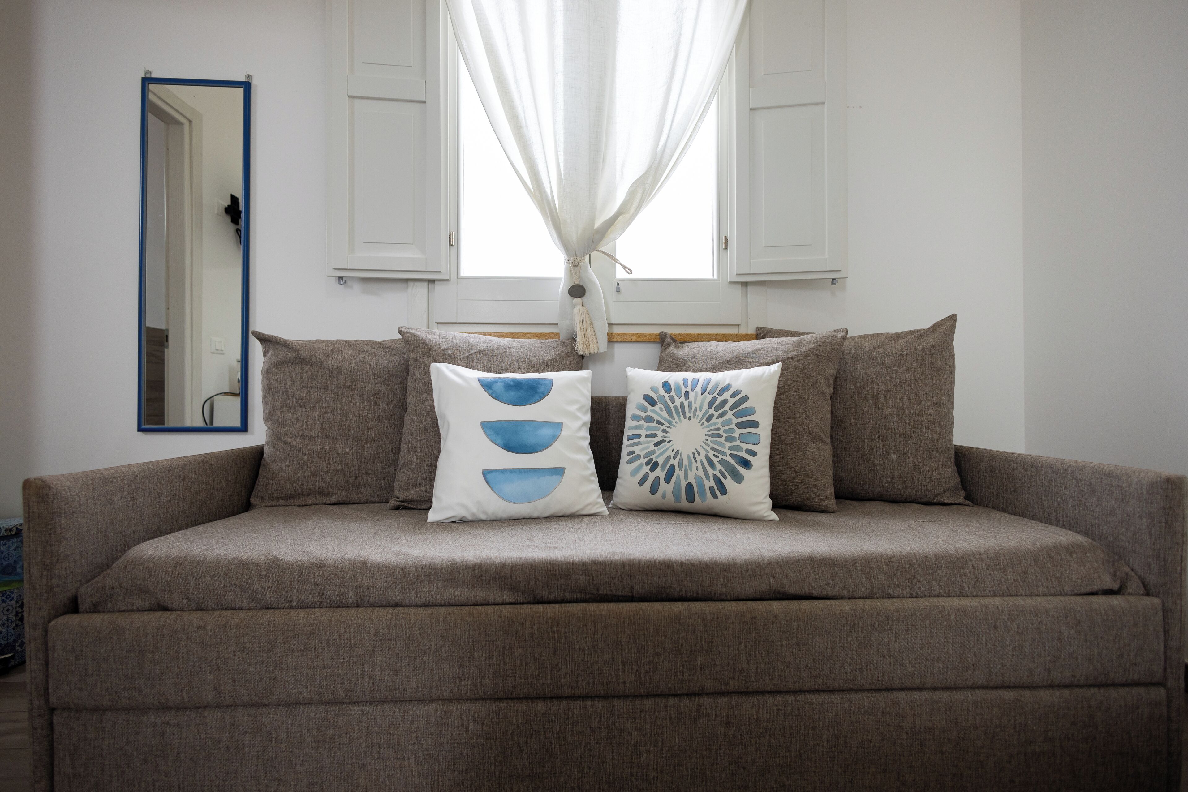Um sofá com duas almofadas decorativas, um espelho e uma janela com persianas brancas.