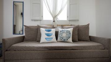 Um sofá com duas almofadas decorativas, um espelho e uma janela com persianas brancas.