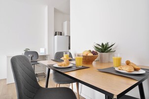 Disposição para o pequeno-almoço com croissants, sumo de laranja e uma saladeira de fruta sobre uma mesa de madeira.