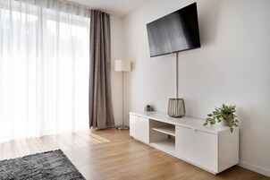 Uma sala de estar moderna com uma televisão de tela plana na parede, uma mesinha console branca com uma planta e um abajur.