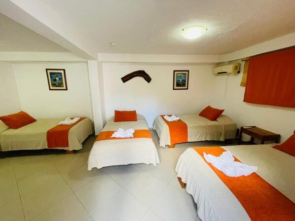 Quarto de hotel com quatro camas de solteiro, cada uma com colcha branca e laranja, e cortina vermelha na parede da direita.
