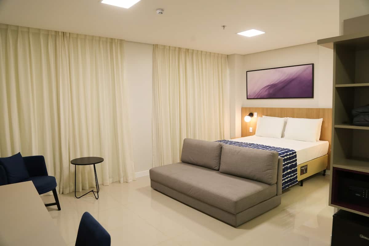 Quarto de hotel com cama, sofá, mesa pequena e televisão.