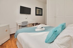 Quarto de hotel com cama, escrivaninha, cadeira, televisão e guarda-roupa.