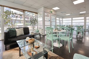 Um interior moderno com sofá preto, mesa de centro de vidro, cadeiras verde-água e janelas amplas com vista para o exterior.