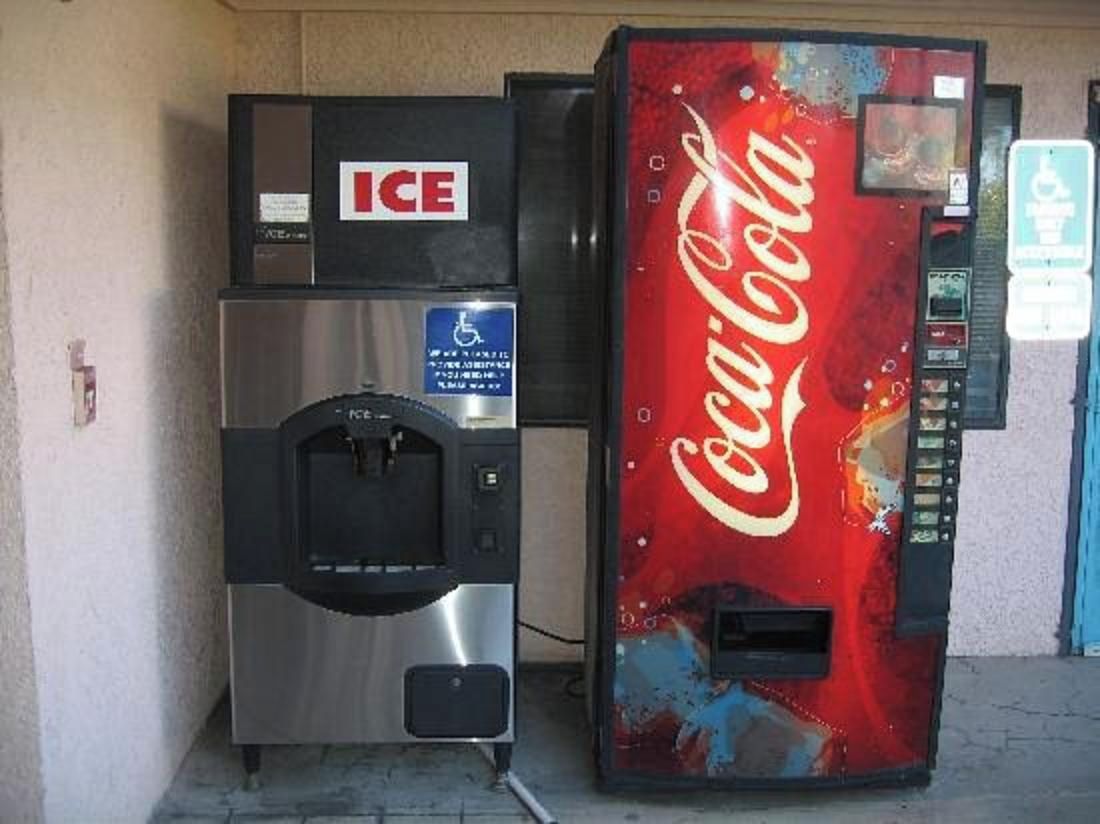 Máquina de vendas com logotipos ICE e Coca-Cola, ambas com sinalização de acessibilidade para pessoas com deficiência.