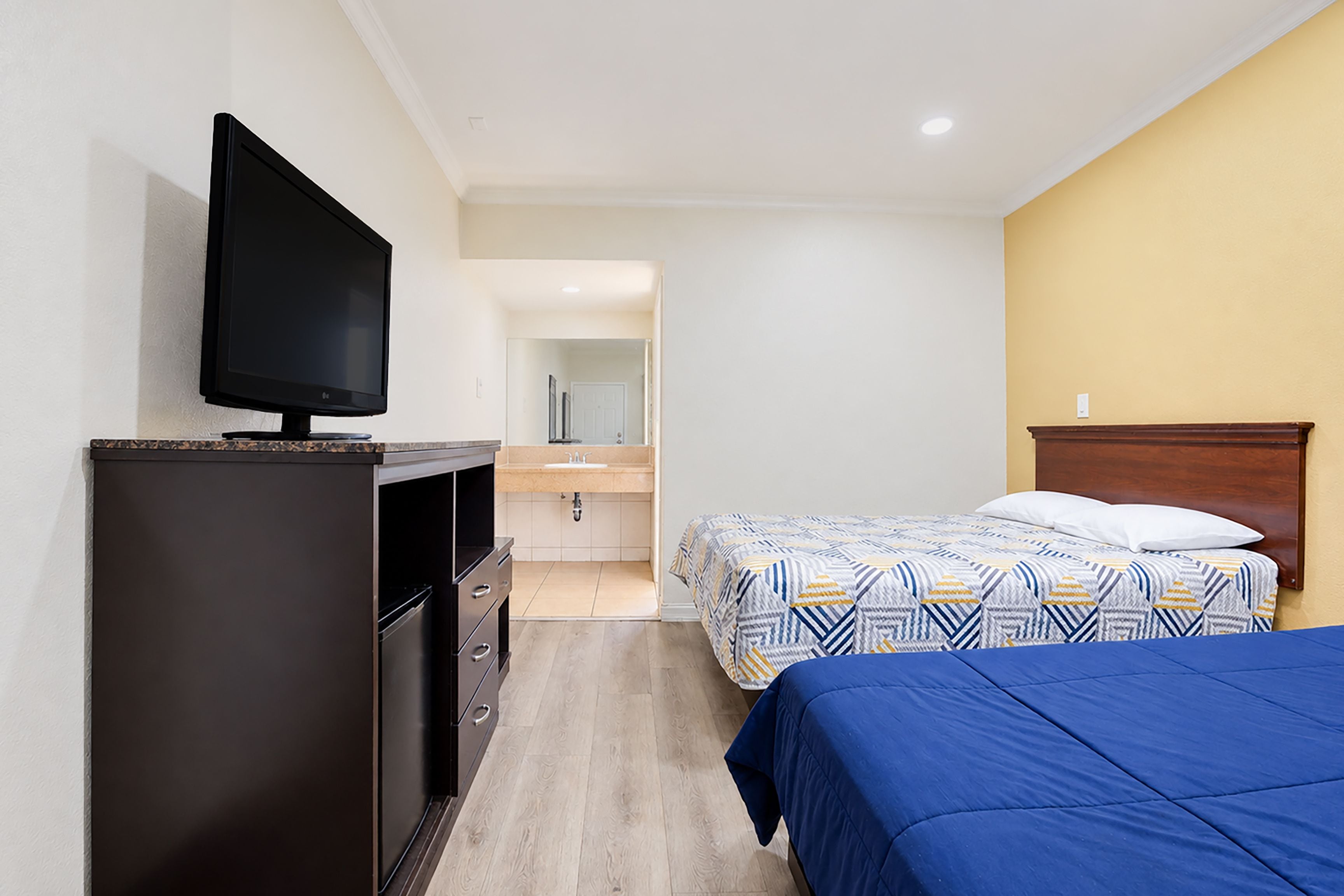 Quarto de hotel com uma cama, televisão em uma cômoda, banheiro com espelho e cabeceira de madeira.
