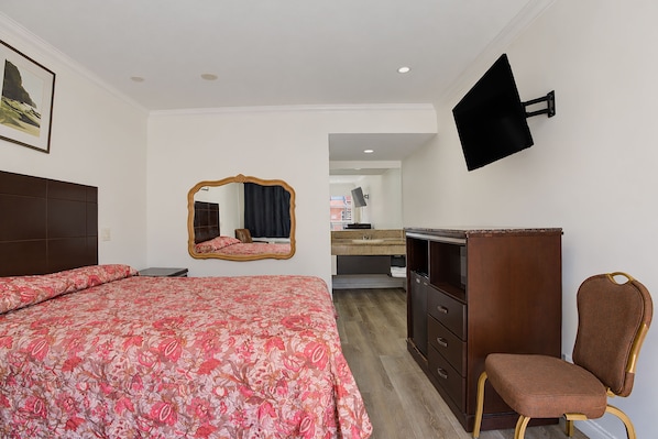 Quarto de hotel com cama, televisão, espelho, escrivaninha e cadeira.