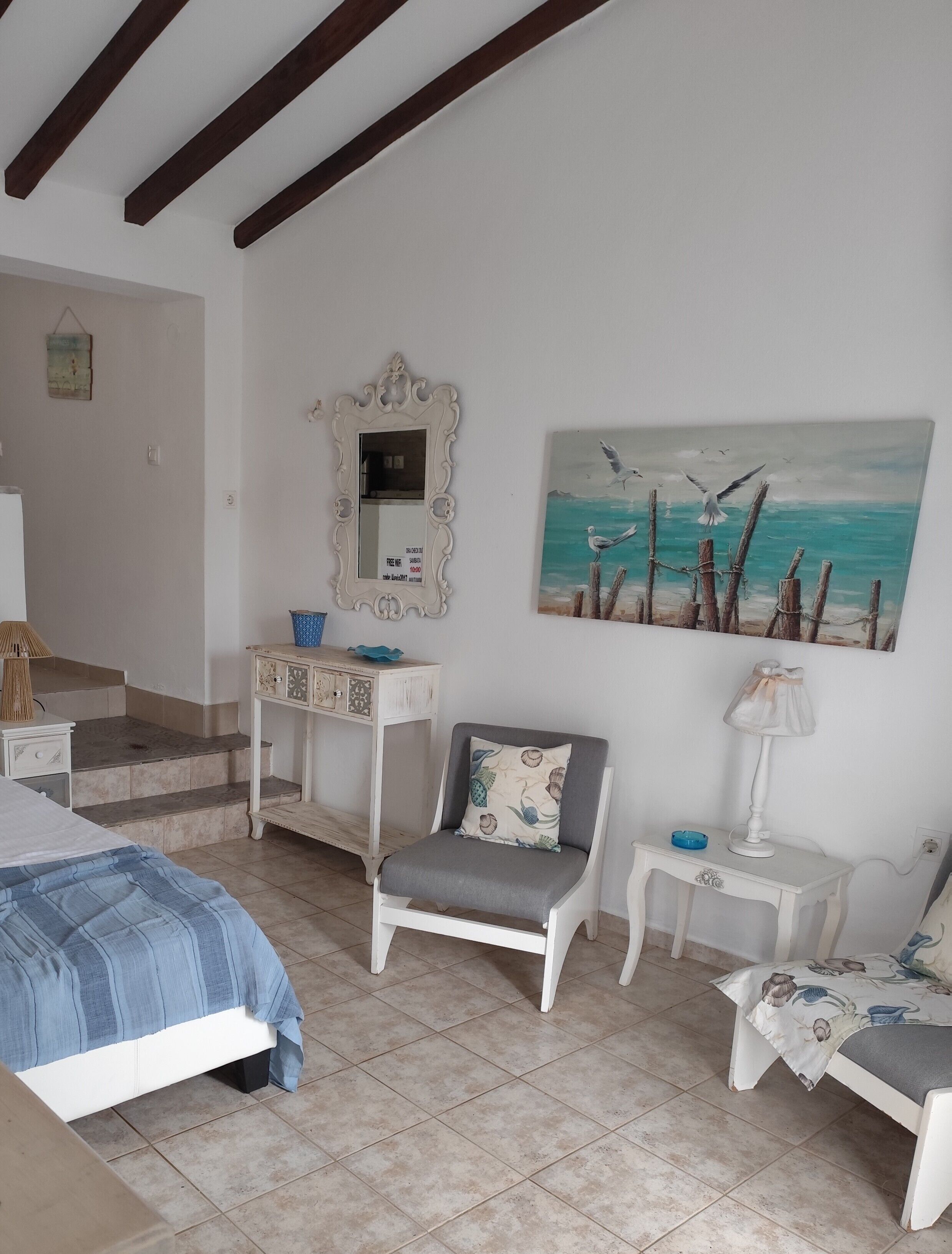 Um quarto com uma cama, uma cadeira, uma mesinha, uma luminária e um quadro na parede.