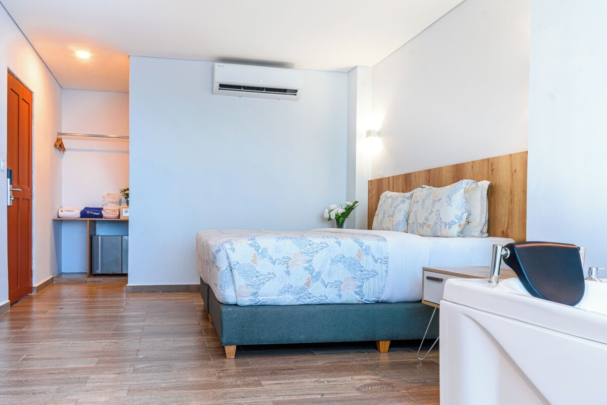 Quarto de hotel com uma cama, mesa de cabeceira, escrivaninha e ar condicionado.