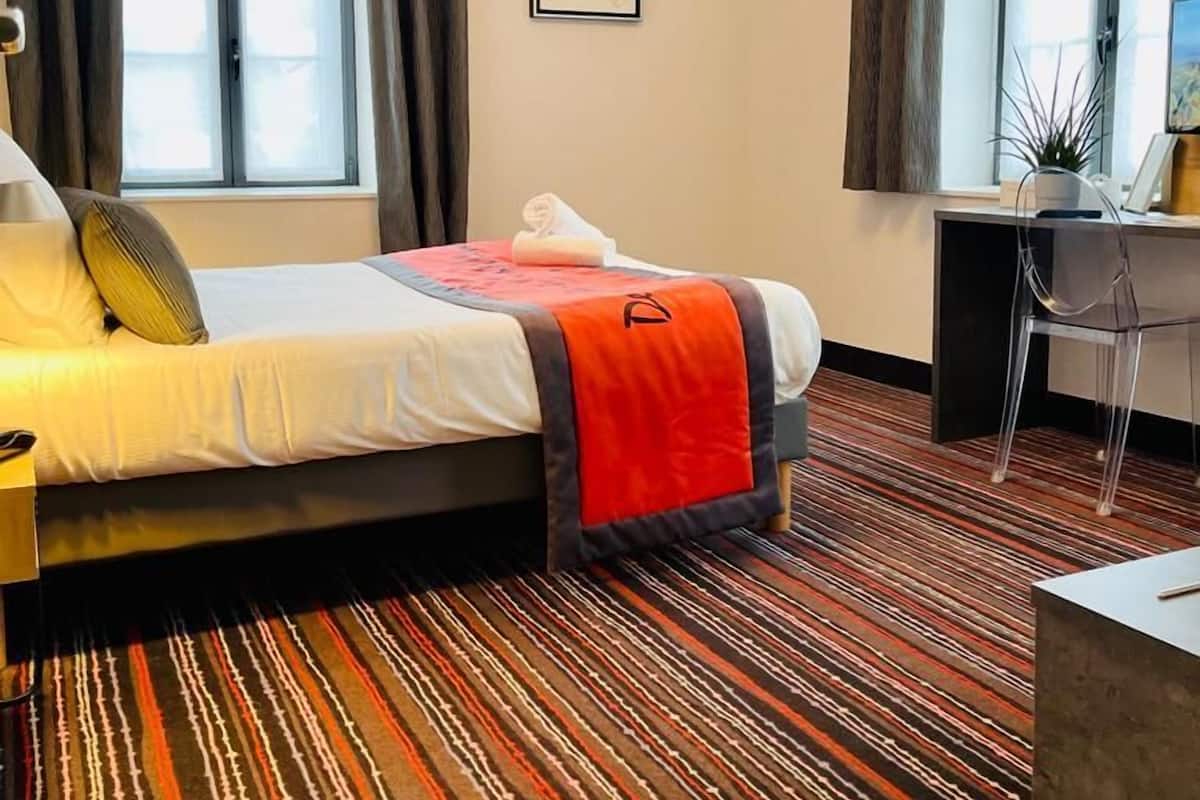 Quarto de hotel com cama, escrivaninha e cadeira.