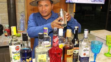 Um bartender segurando um coqueteleira com diversas garrafas de álcool e copos sobre o balcão.